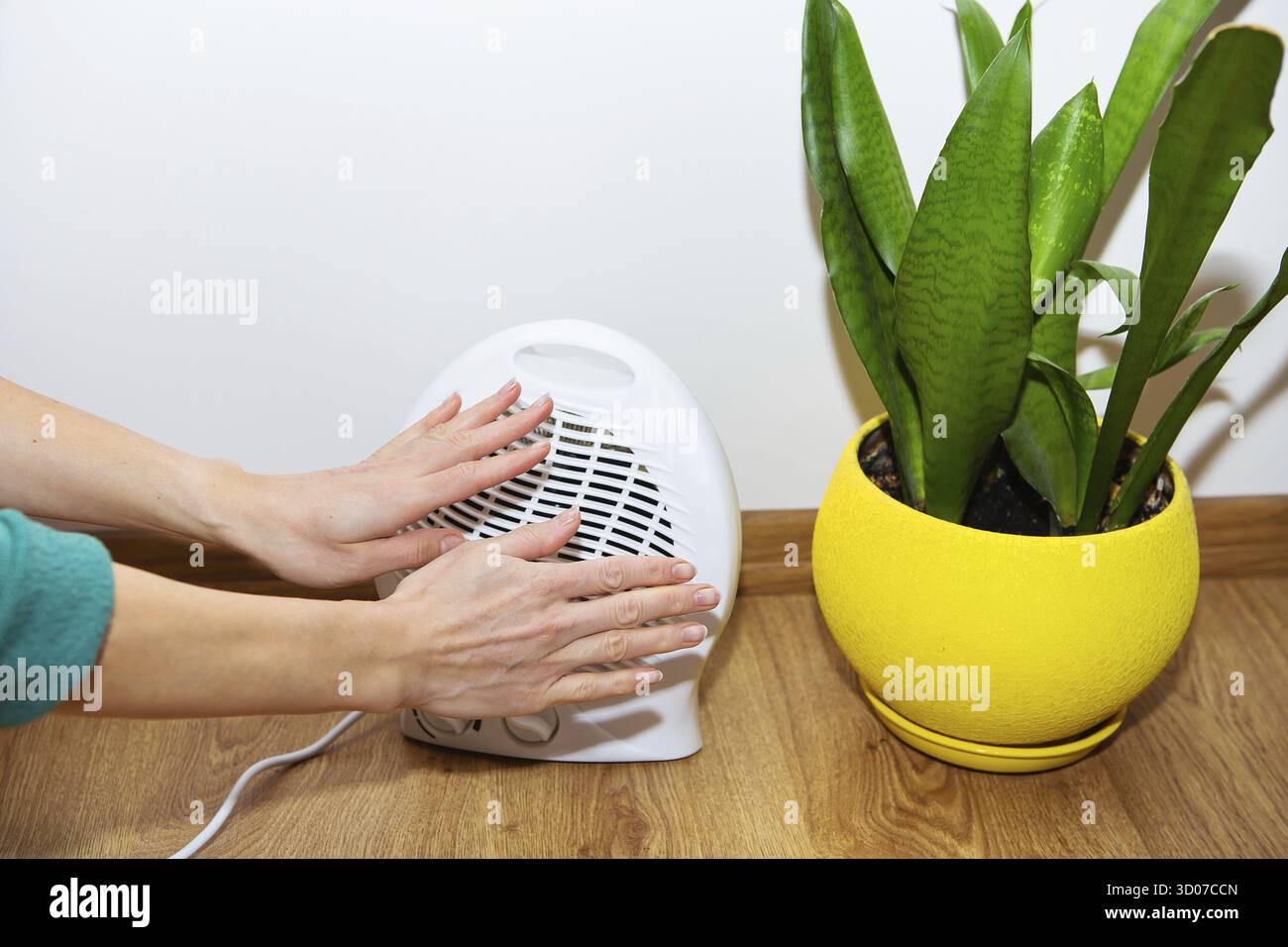 The girl holds her hands near a plastic fan heater and warms her hands ...