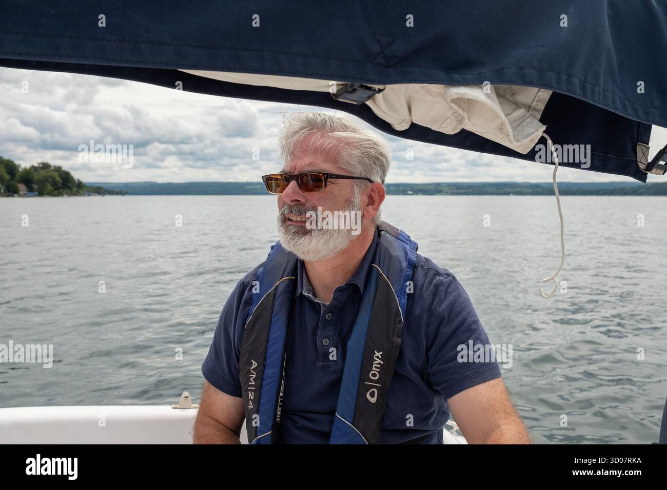 A man sitting under a boom with the mainsail folded above his head. The ...
