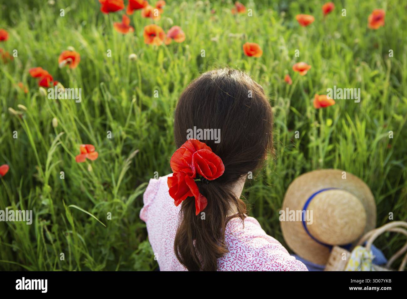 A woman sits in a poppy field, adorned with poppy flowers in her hair ...