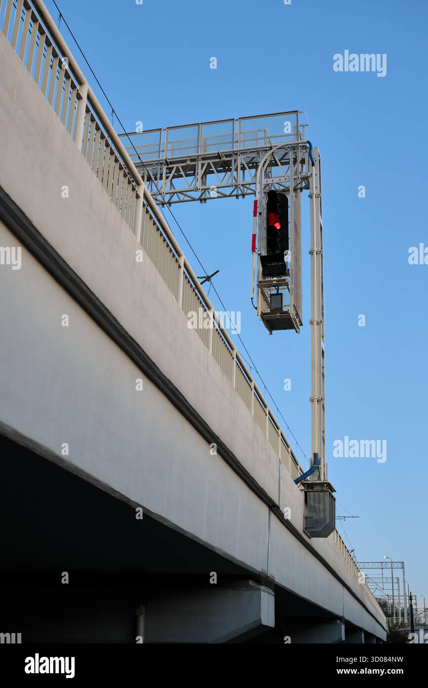 Red railway signal light on a modern bridge structure against clear ...