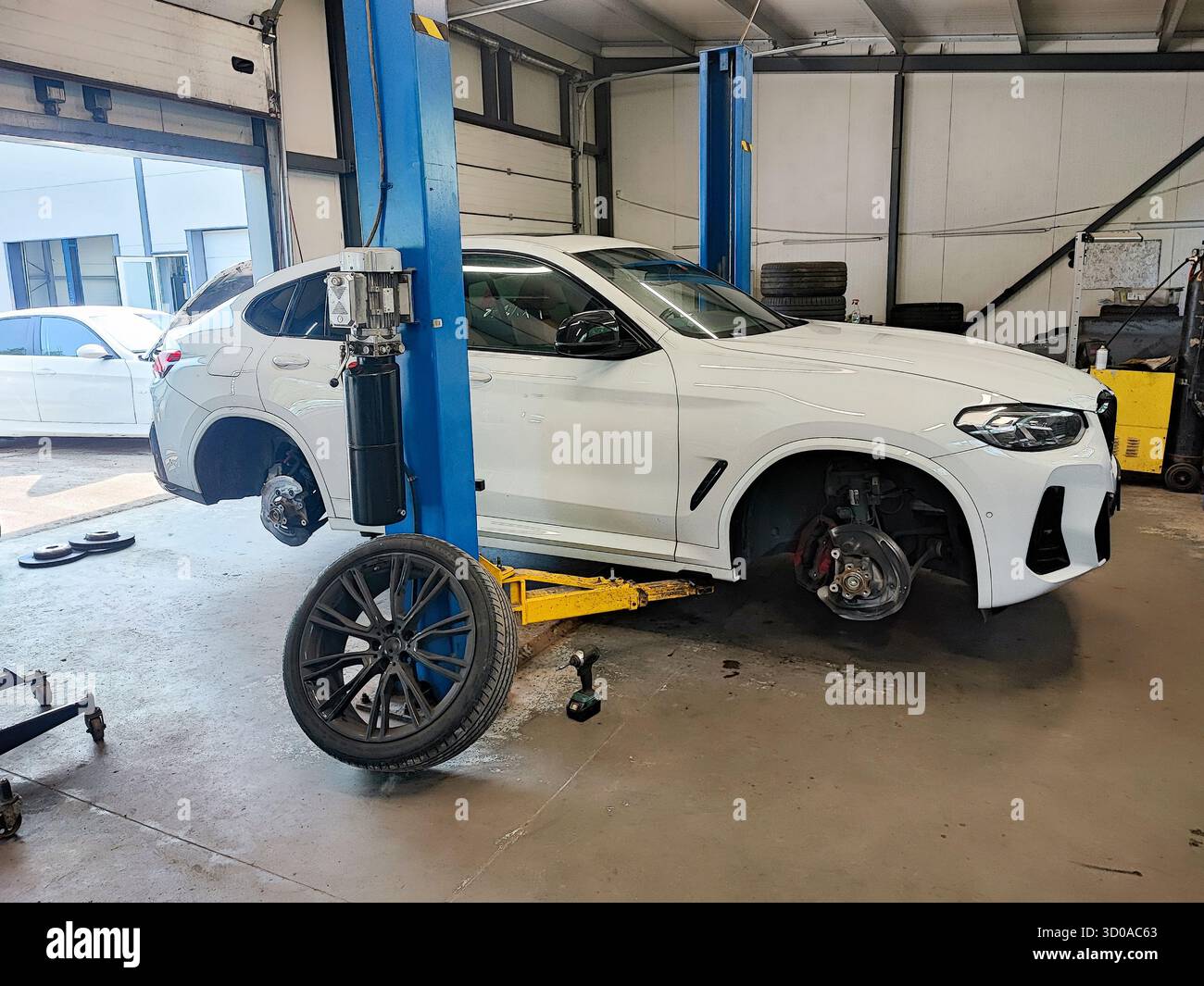 White modern SUV without wheels lifted on car service hoist during ...