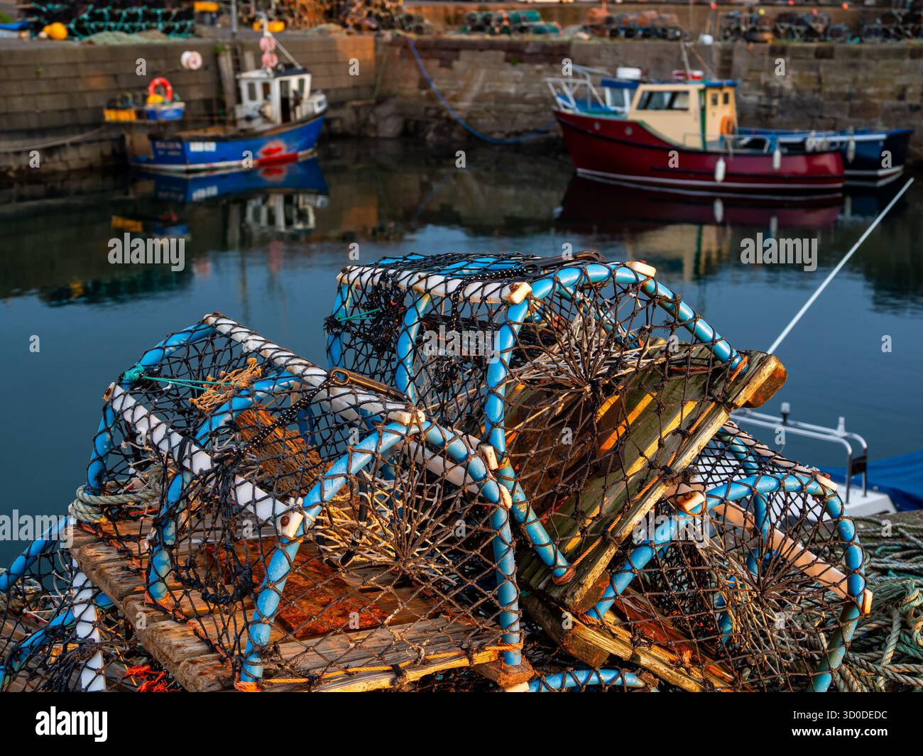 Lobster pots stacked on the quayside with fishing boats in St Abbs ...