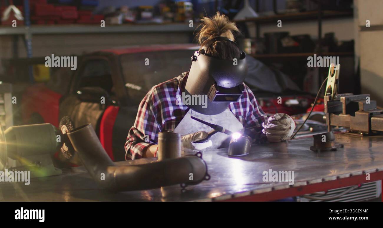 Female welder welding metal pipe sections at repair workshop, with ...