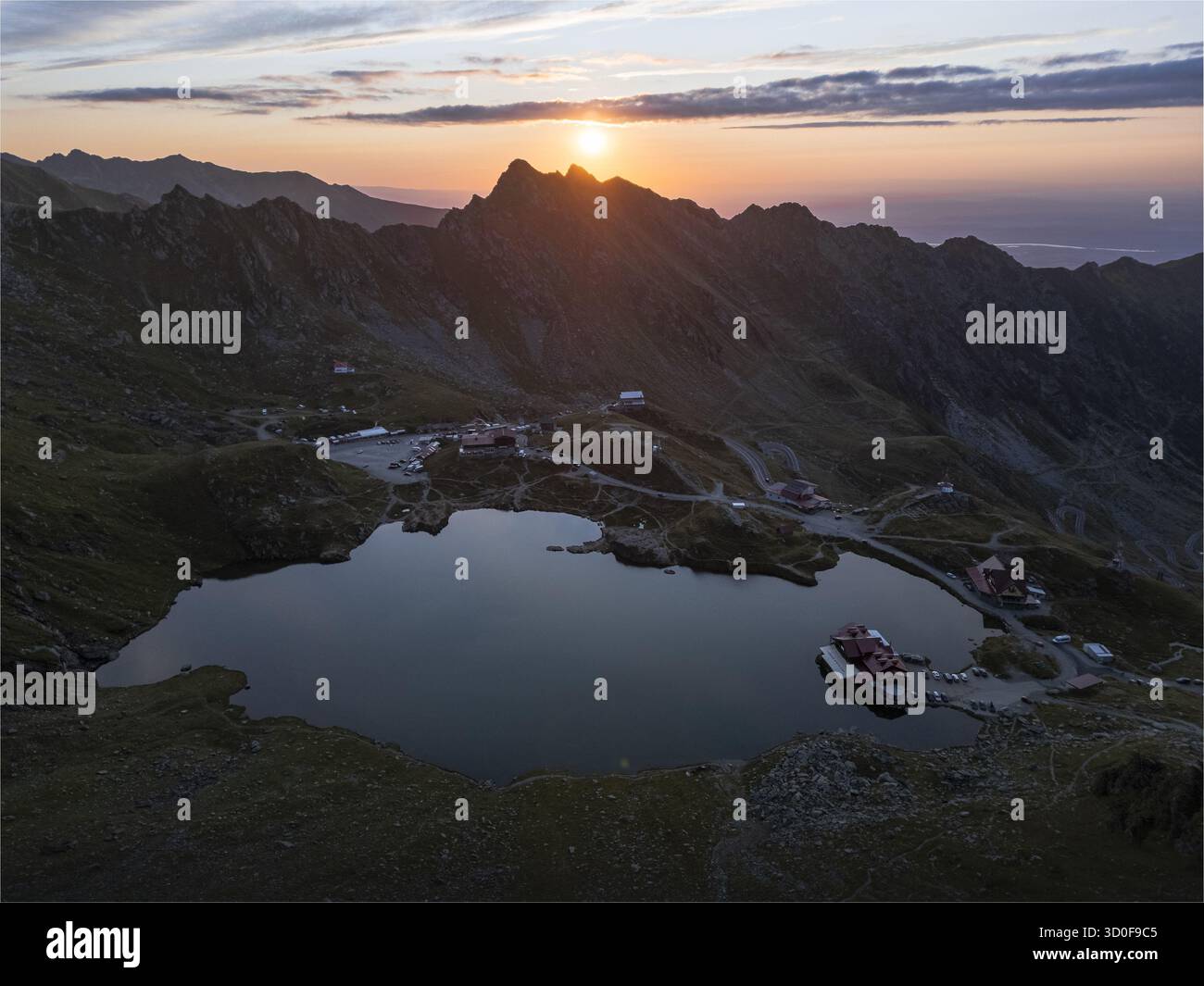 Aerial view of a serene lake mirroring the fiery sunset amidst jagged ...