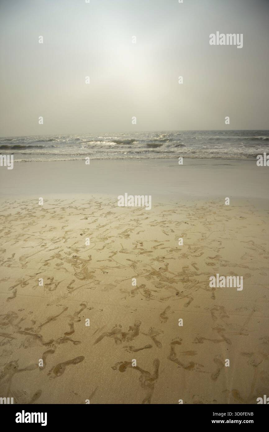 Many footprints on the sand at the ocean beach. Vertical photo with ...