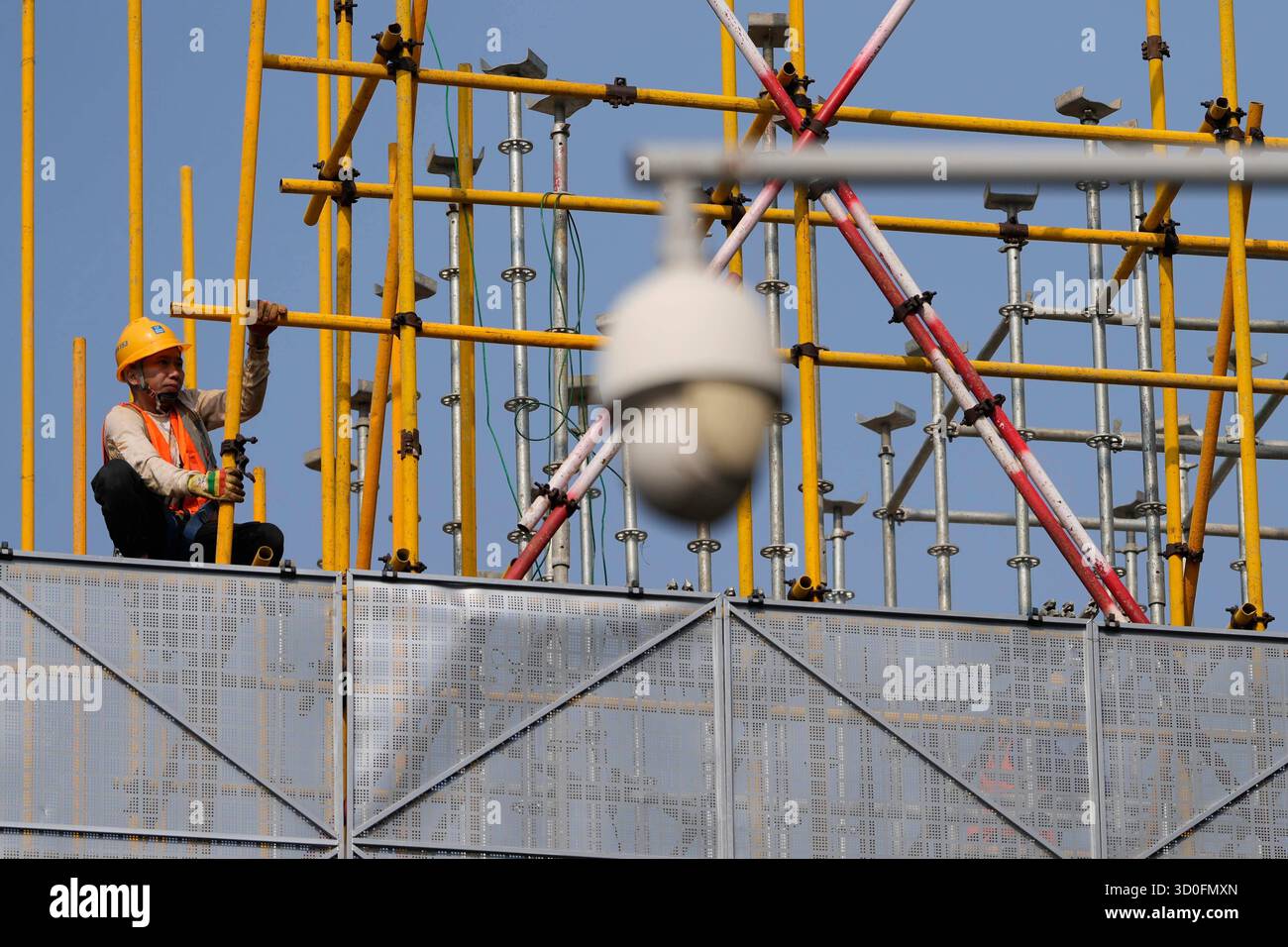 A worker labors on a buildingn rear a security camera in Beijing, China ...