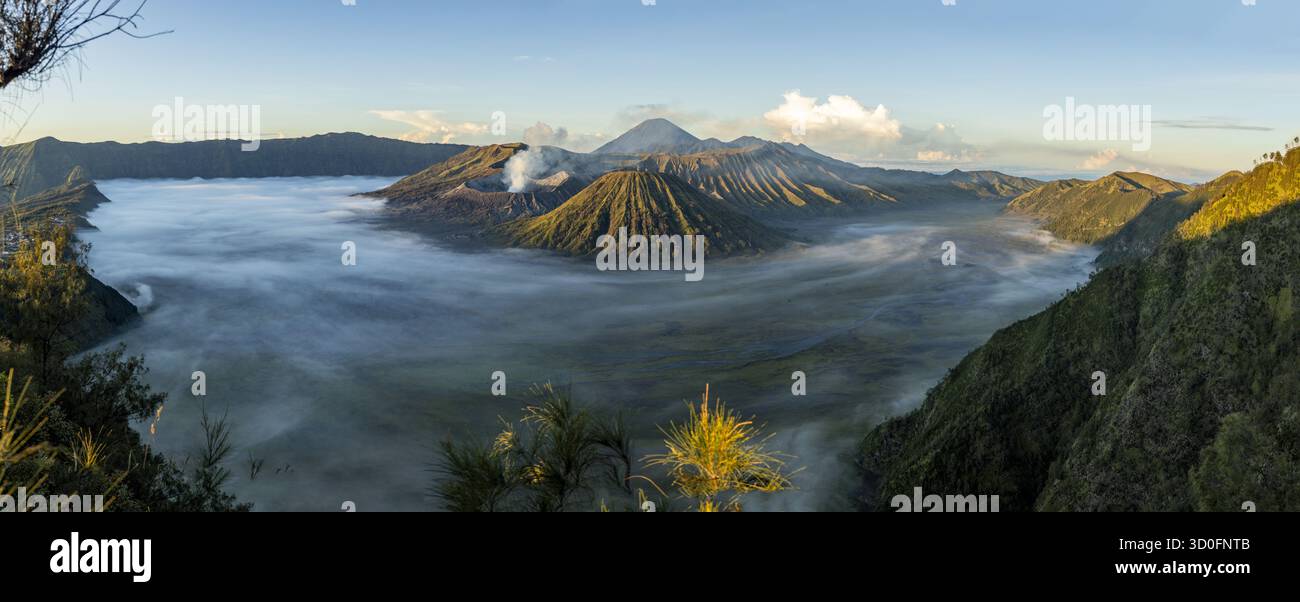 View of mist-shrouded volcanic landscape with smoking peaks piercing ...