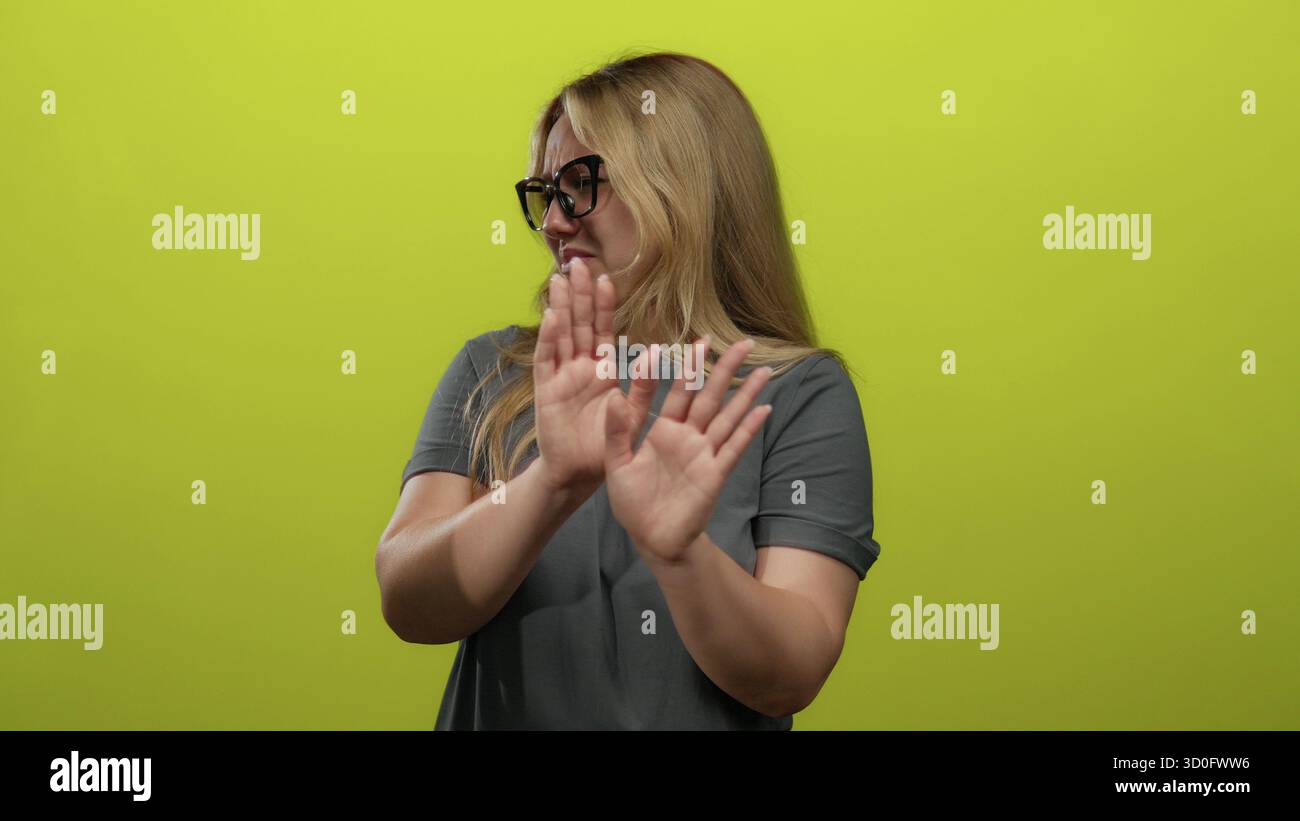 Woman expressing disgust with hands raised in front of isolated green ...