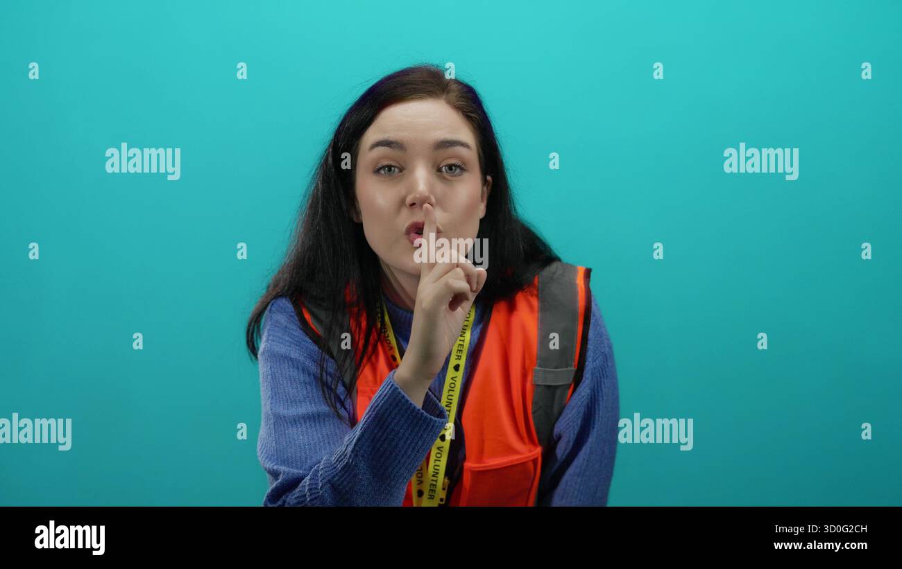 Woman gesturing silence wearing volunteer vest against blue background ...
