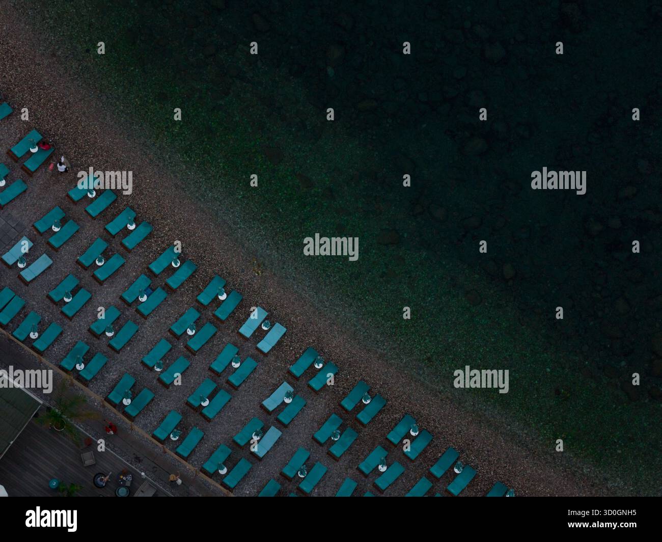 Aerial view of turquoise sunbeds aligned on the beach next to the dark ...