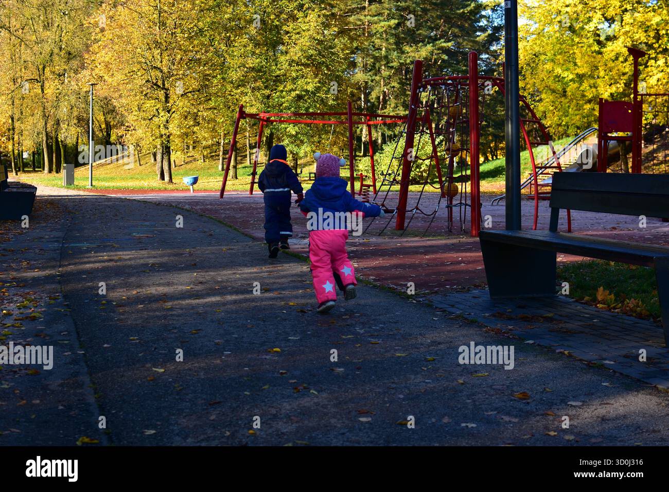 Two children in warm overalls running toward playground with swings and ...