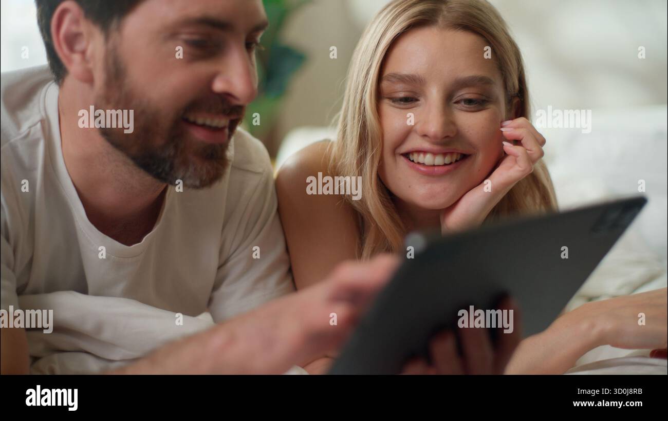 Smiling Caucasian family couple in love use tablet apps in bedroom ...