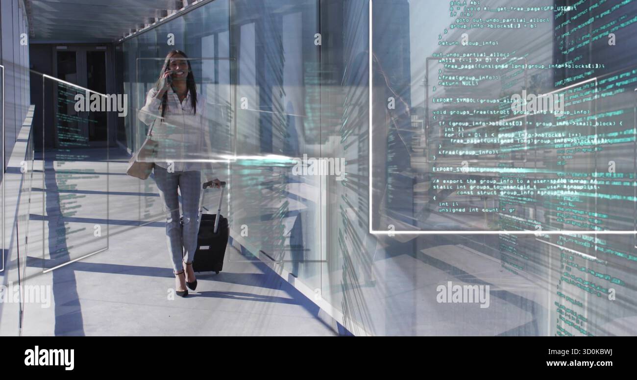 Walking executive pulling suitcase, talking on smartphone through glass ...