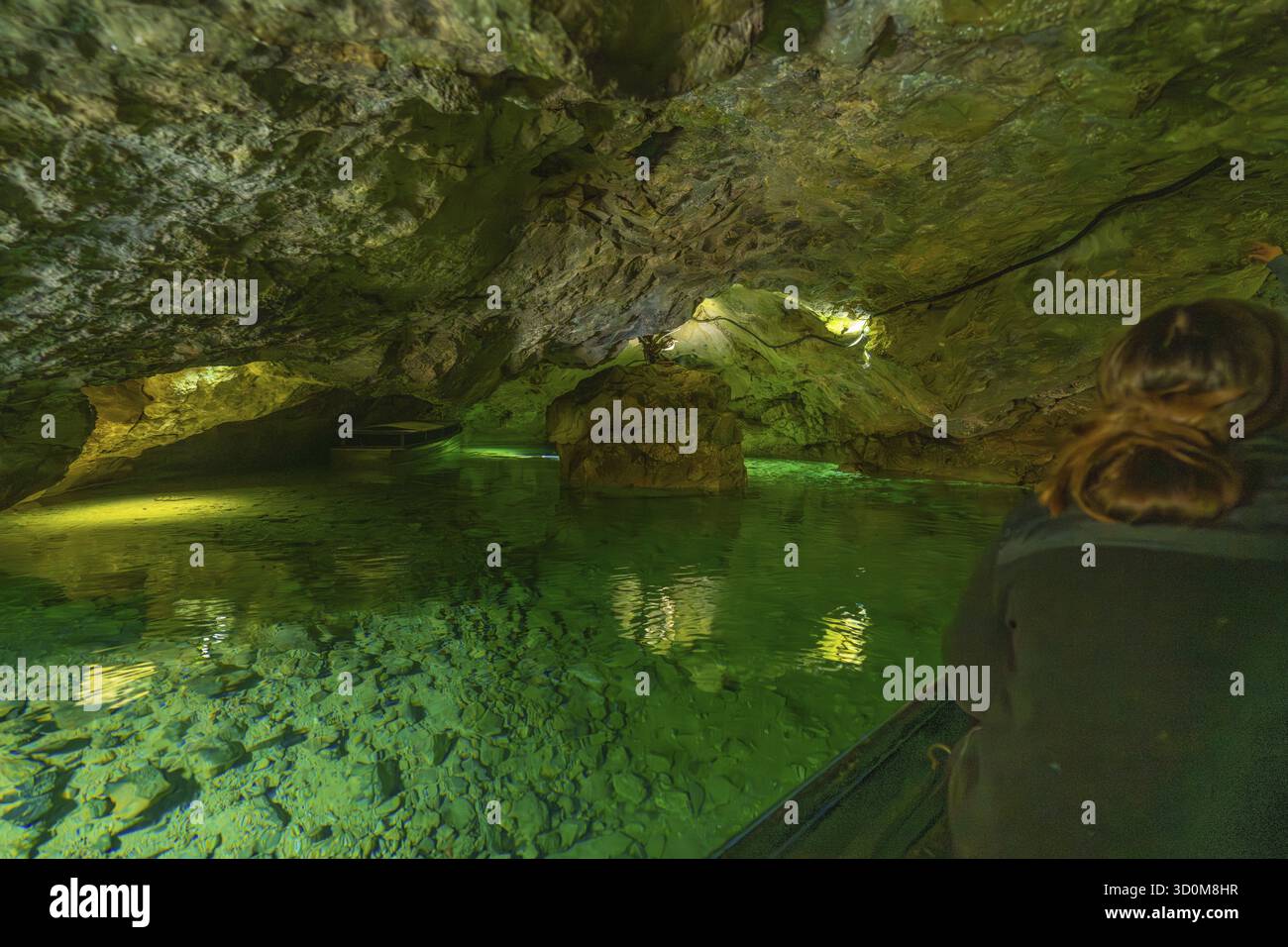 Interior of a cave with green water and rocks, people exploring the ...