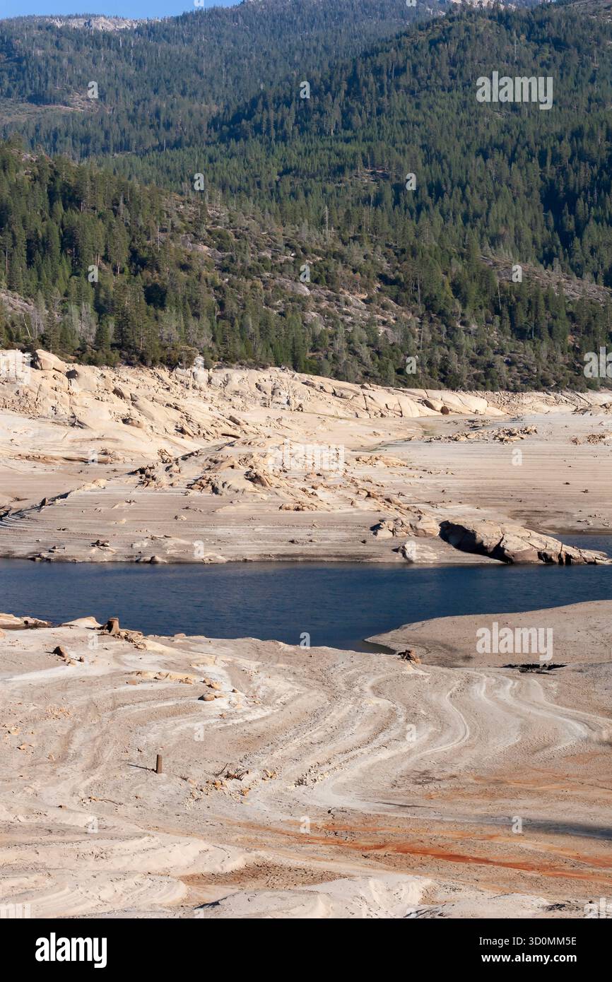 Dried reservoir with exposed lakebed and forested mountain backdrop ...