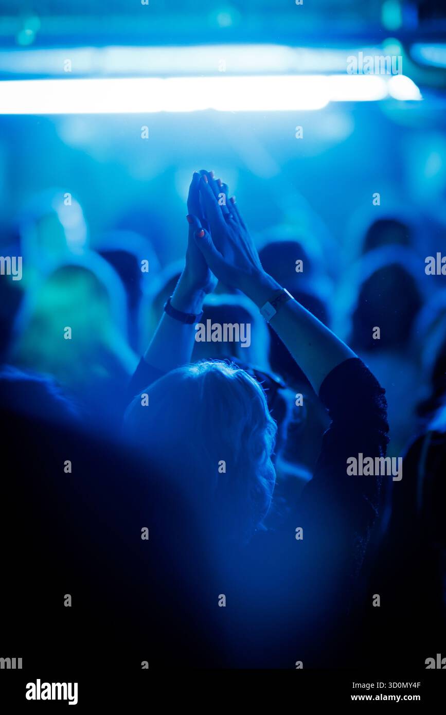 Woman raising hands and clapping among audience during live concert ...