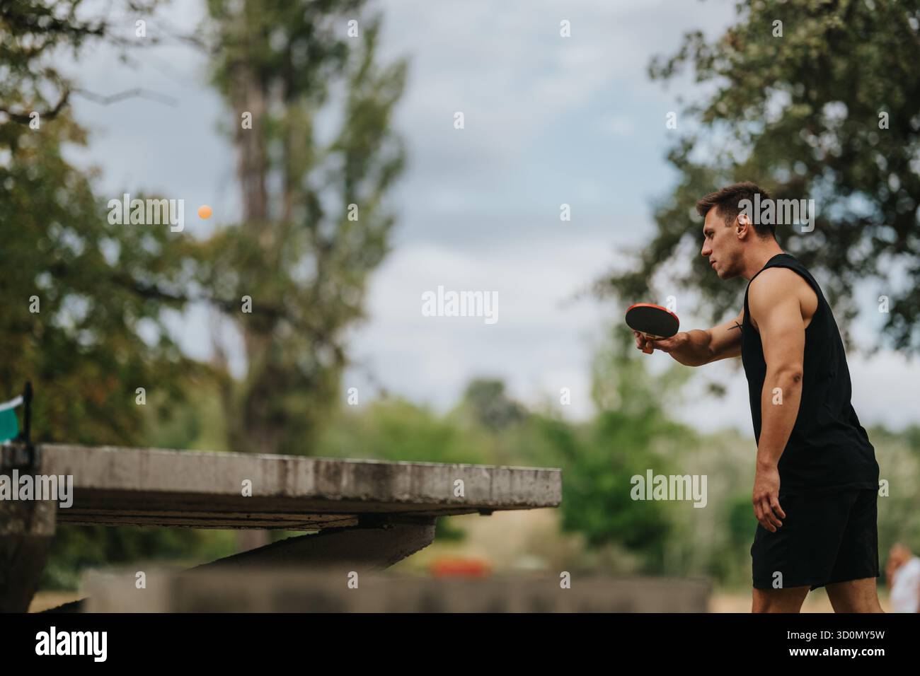 Man in black athletic wear serves a ping pong ball outdoors on a park ...
