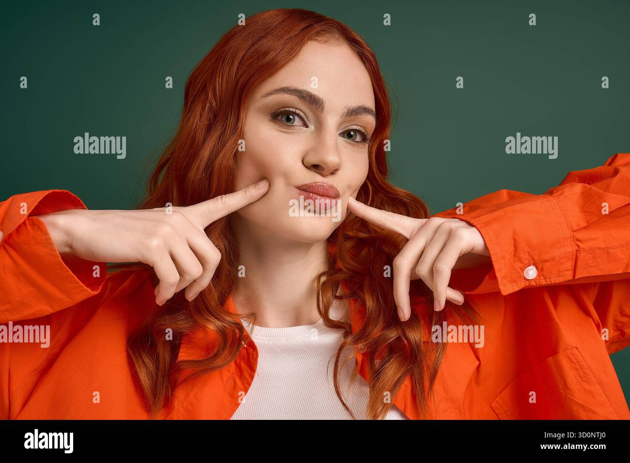 Young woman playfully poses with her fingers on her cheeks, wearing a ...