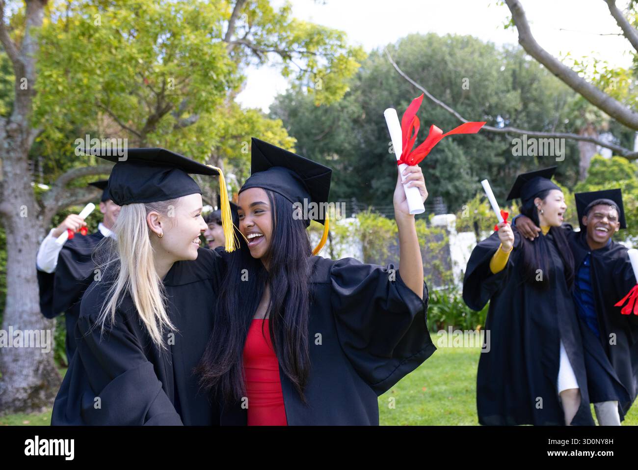 Graduating students outdoors in caps and gowns, joyfully holding ...