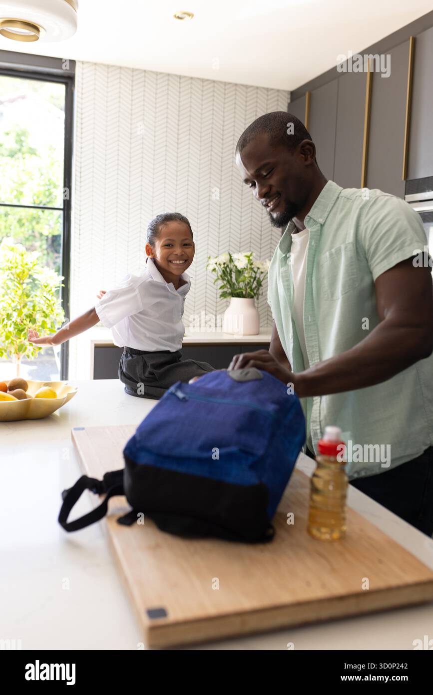 African American father packing school lunch while daughter smiles in ...