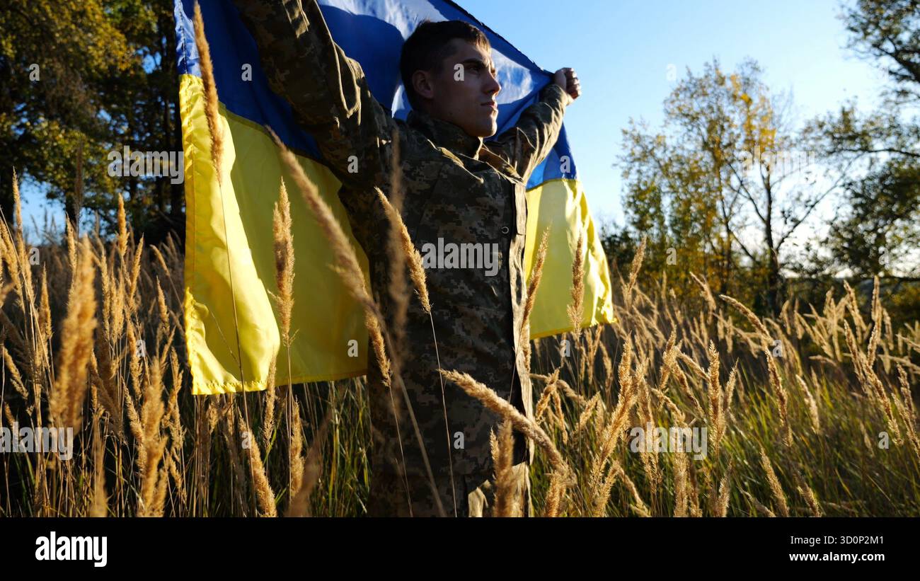 Military man in uniform stands with raised over head flag of Ukraine at ...