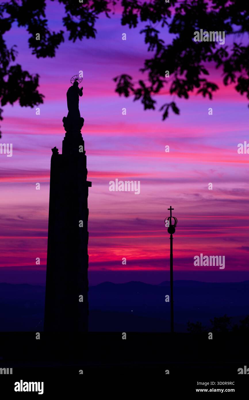 The silhouette of a religious statue stands against a winter sunset ...