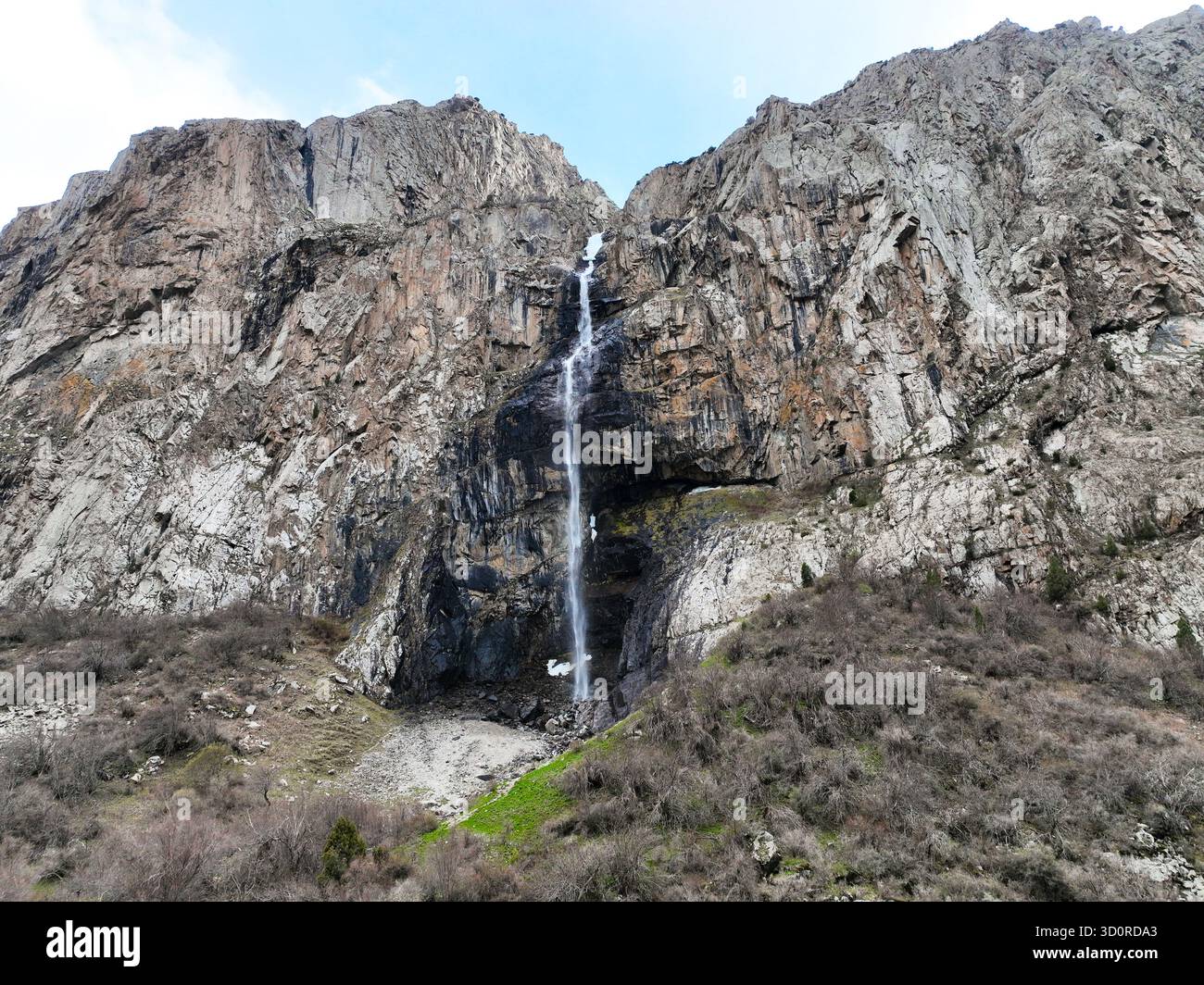 Wide, low-angle view of a thin, tall waterfall dropping from a massive ...