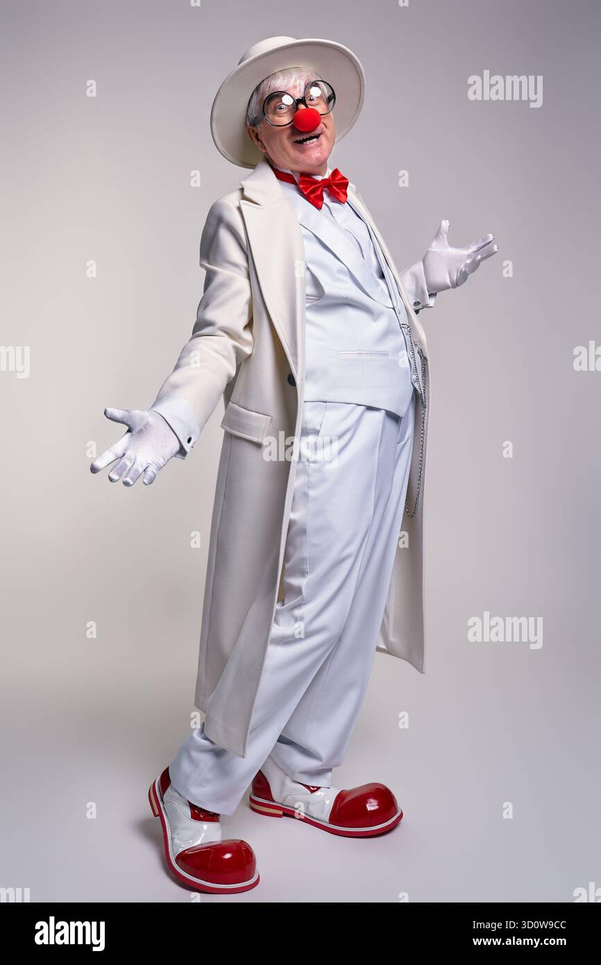 An elderly clown in a white coat and hat. The man is wearing large red ...