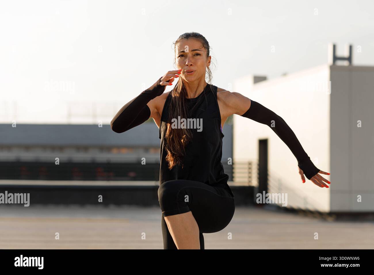 Young slim woman athlete jumping outdoors on the roof, warming up ...