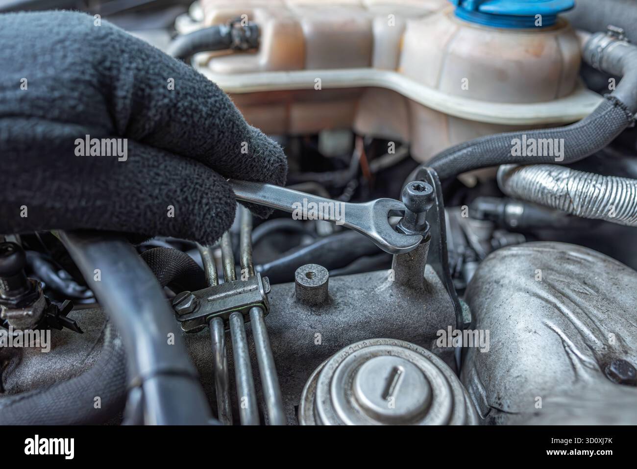 A mechanic wearing a glove using a wrench to tighten a bolt on a car ...