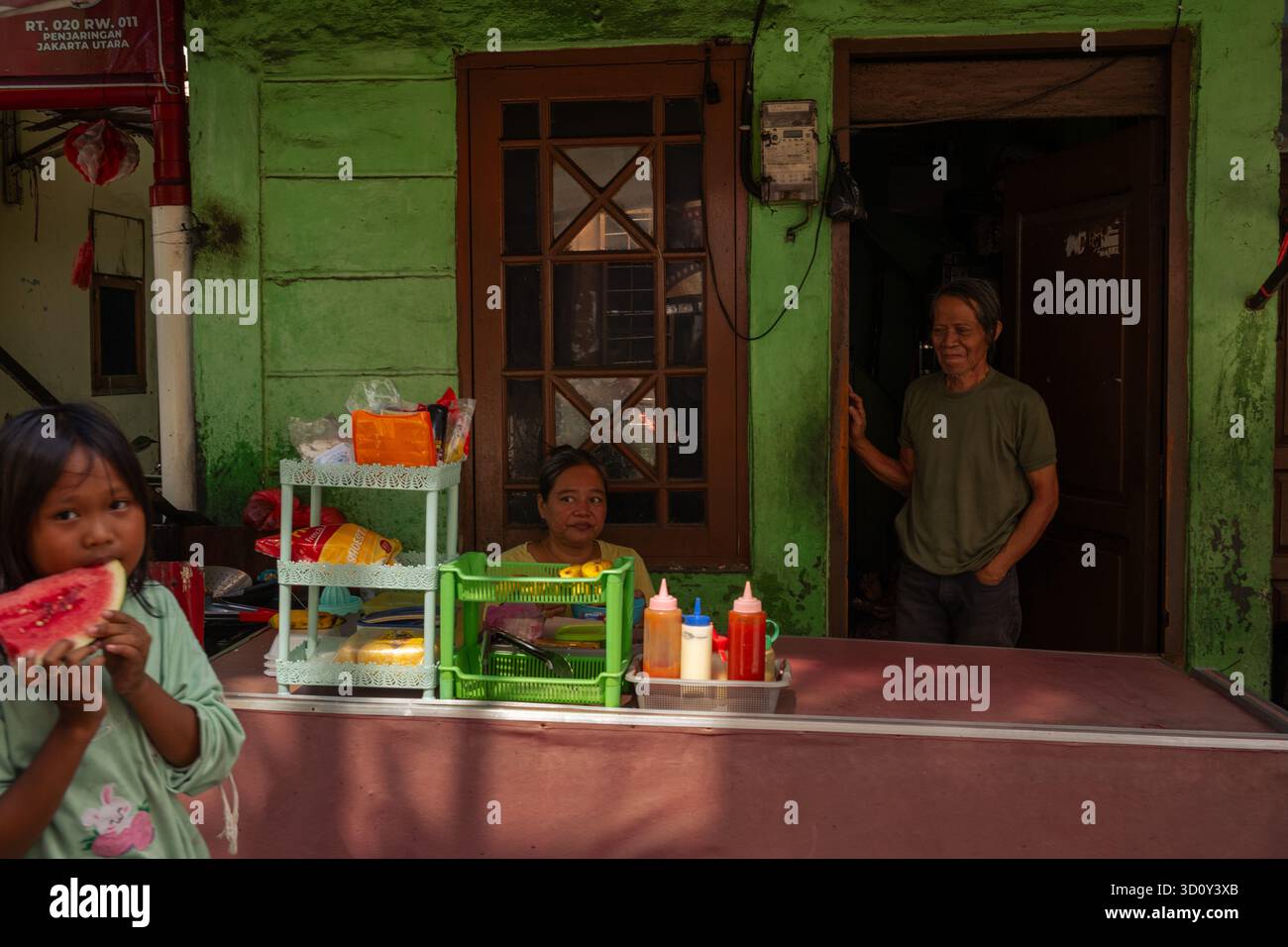 Two food shop owners watch a girl passing by their shop with a piece of ...