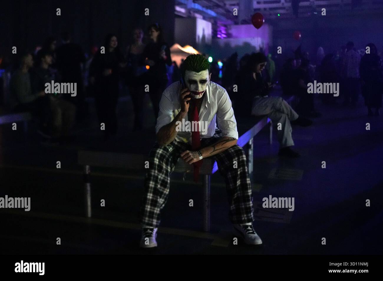 A man dressed as the Joker talks on the phone during a Halloween rave ...