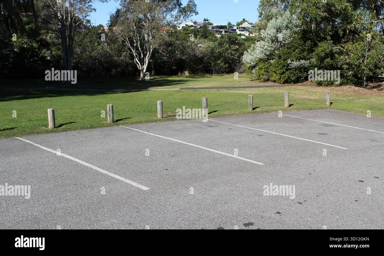Empty parking lot with marked spaces next to a park with trees and ...