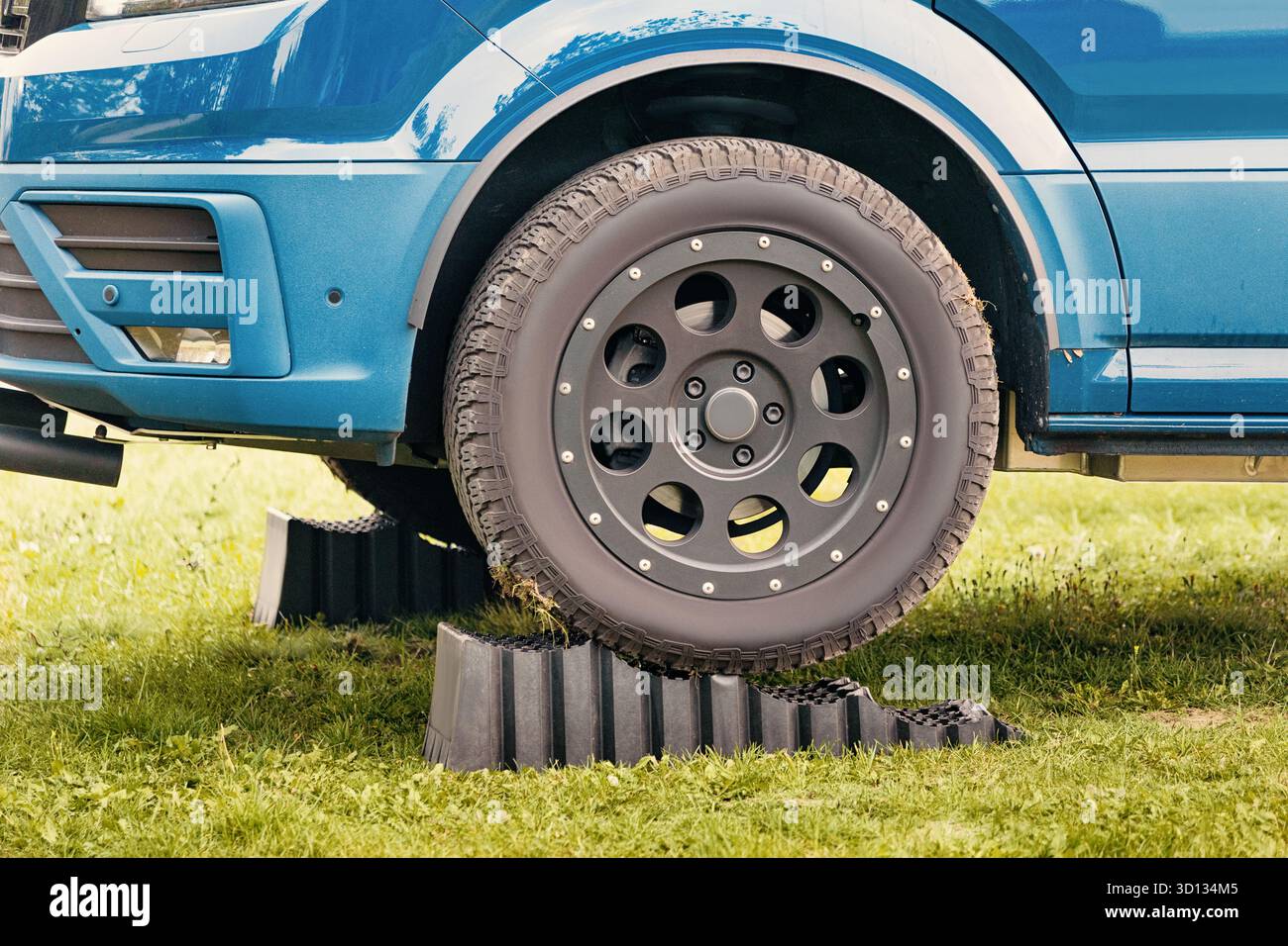 Camper van wheel resting on a leveling block on green grass, ensuring a ...