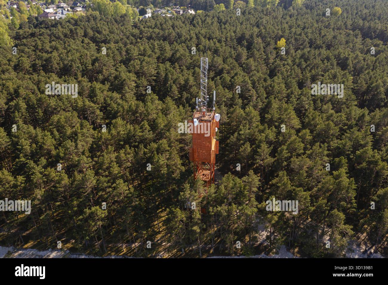 A tall communication tower rises above dense forest canopy on a sunny ...