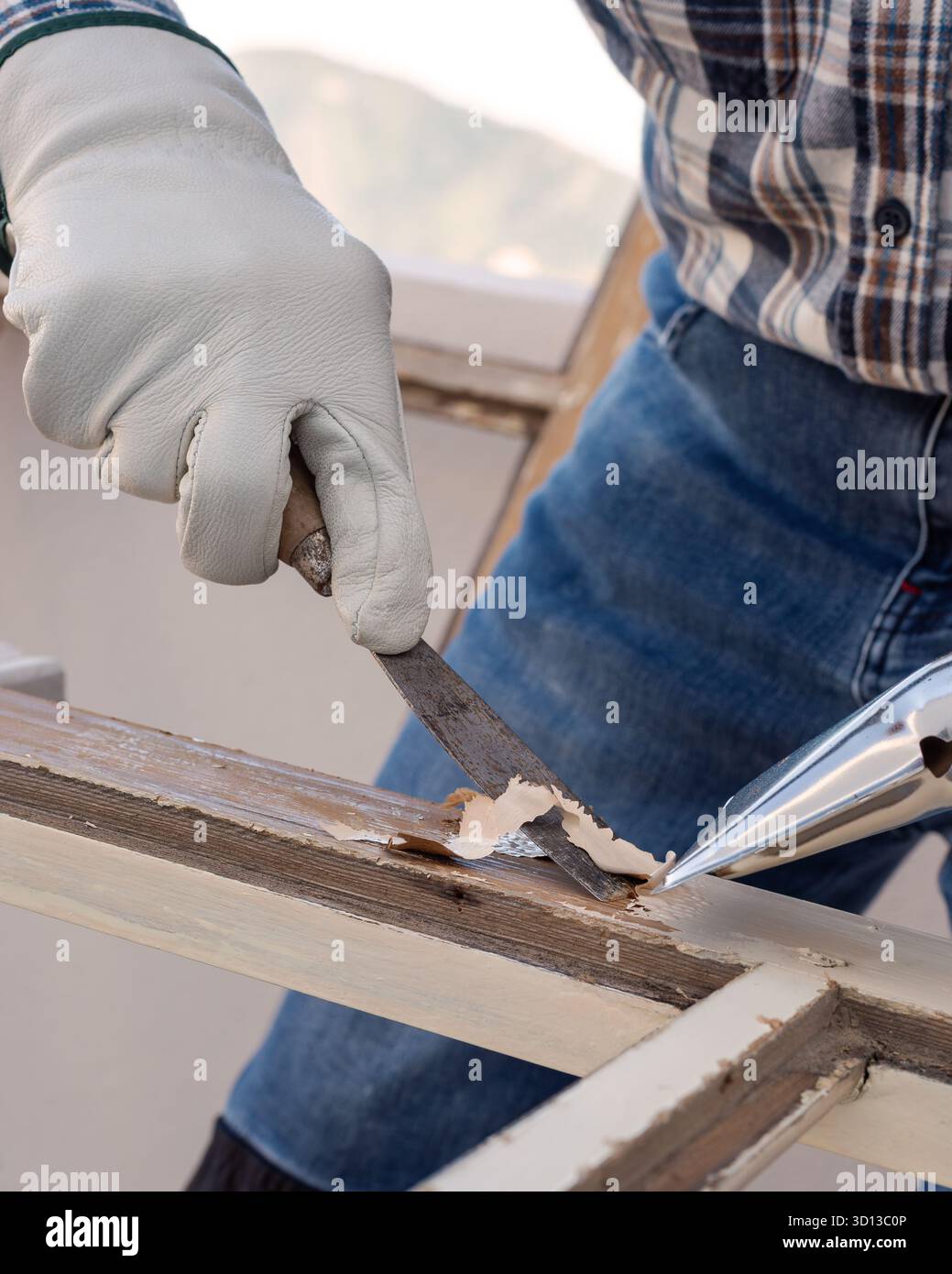Carpenter using heat gun and wood scraper removes paint from old wooden ...