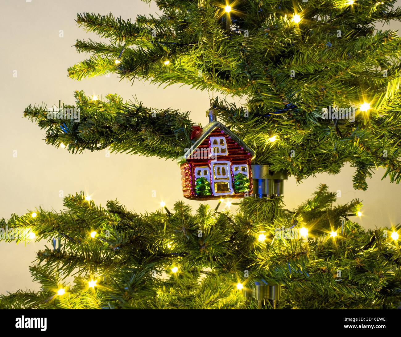 A small red house hangs as a decoration in a lighted Christmas tree ...