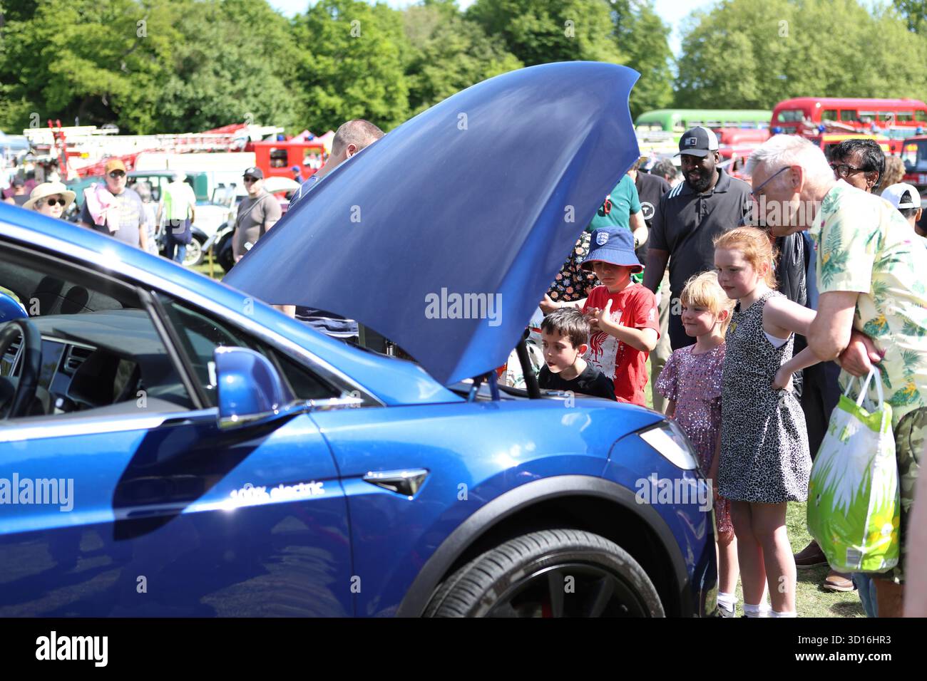 Crowds watching a Tesla Model X car at a vintage car show bonnet up ...