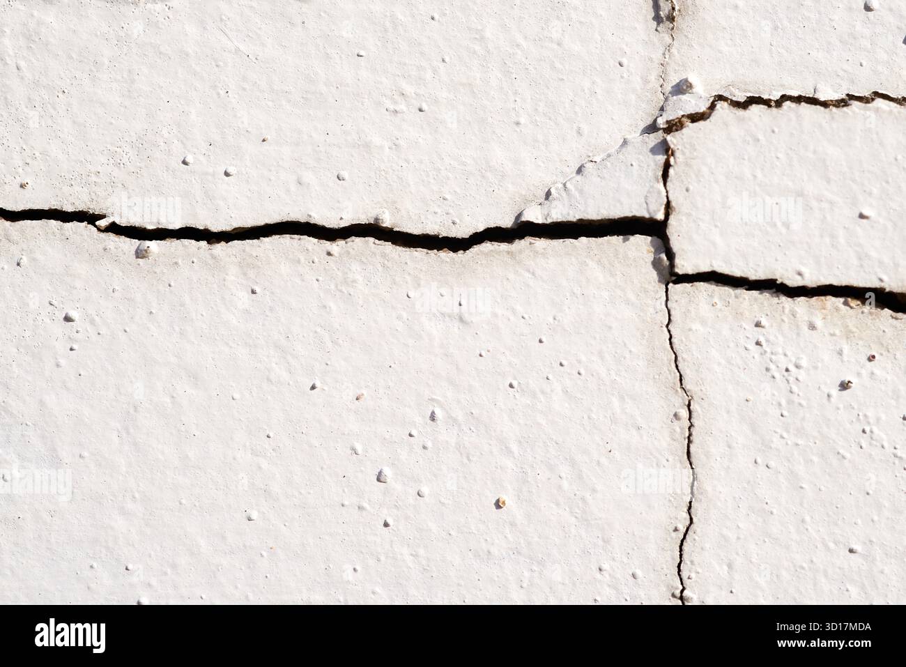 A close-up view of a cracked white wall reveals its wear over time. The ...