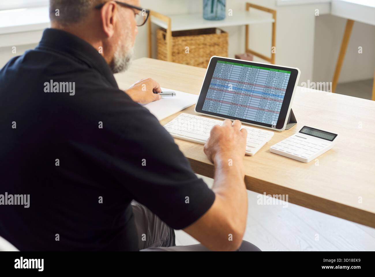 Senior man analyzing spreadsheet on tablet with calculator at tidy home ...