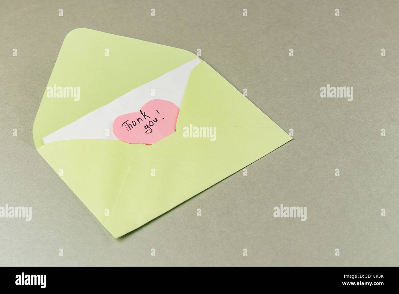 A green envelope rests on a gray surface, revealing a pink heart shape ...