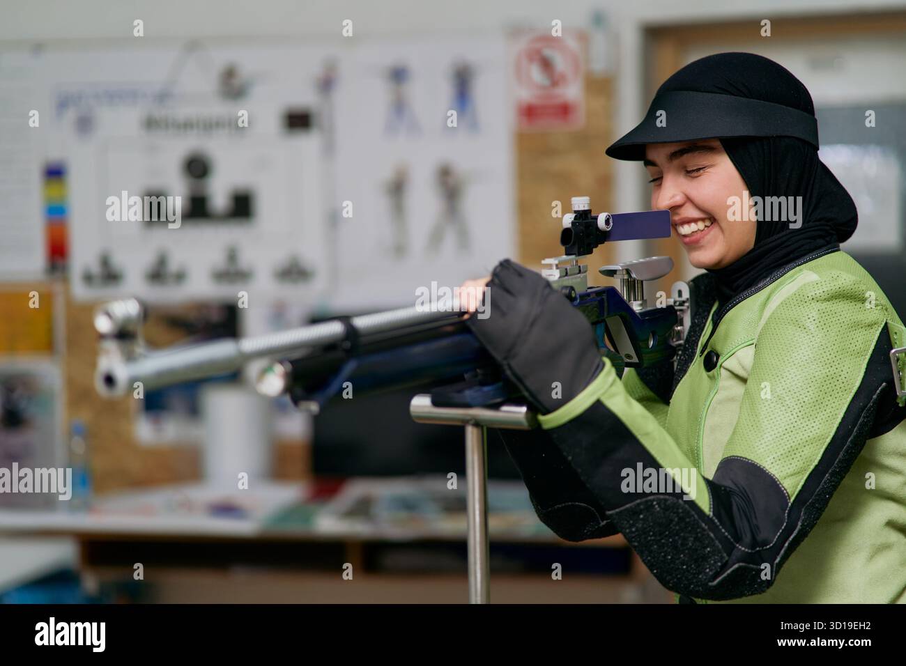 Smiling Muslim woman aiming with air rifle in shooting range, focused ...
