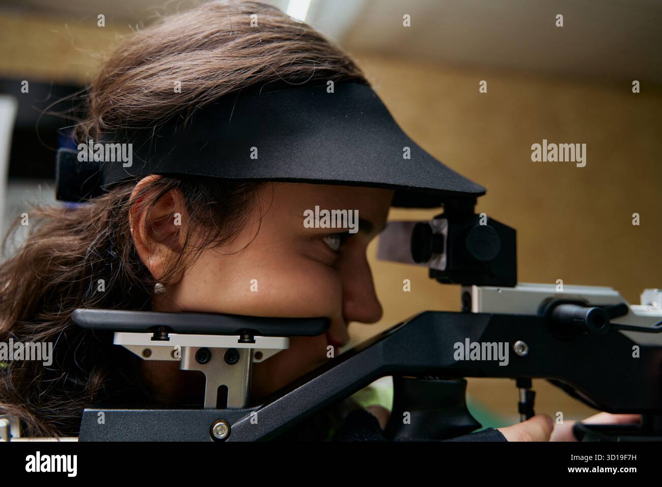 Concentrated woman aiming with air rifle, indoor shooting range ...