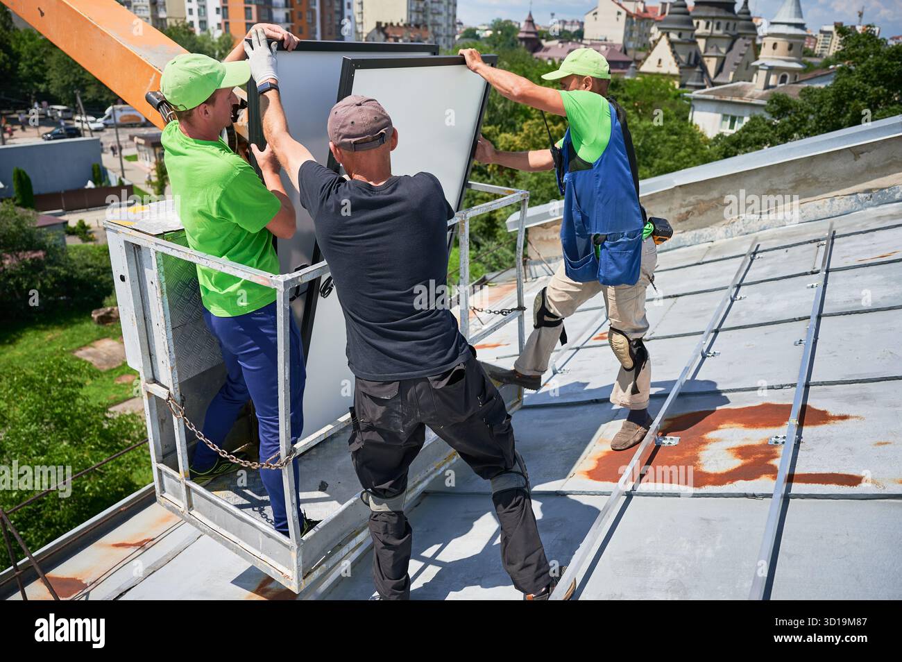 Workers lifting up photovoltaic solar panel on metal rooftop of house ...