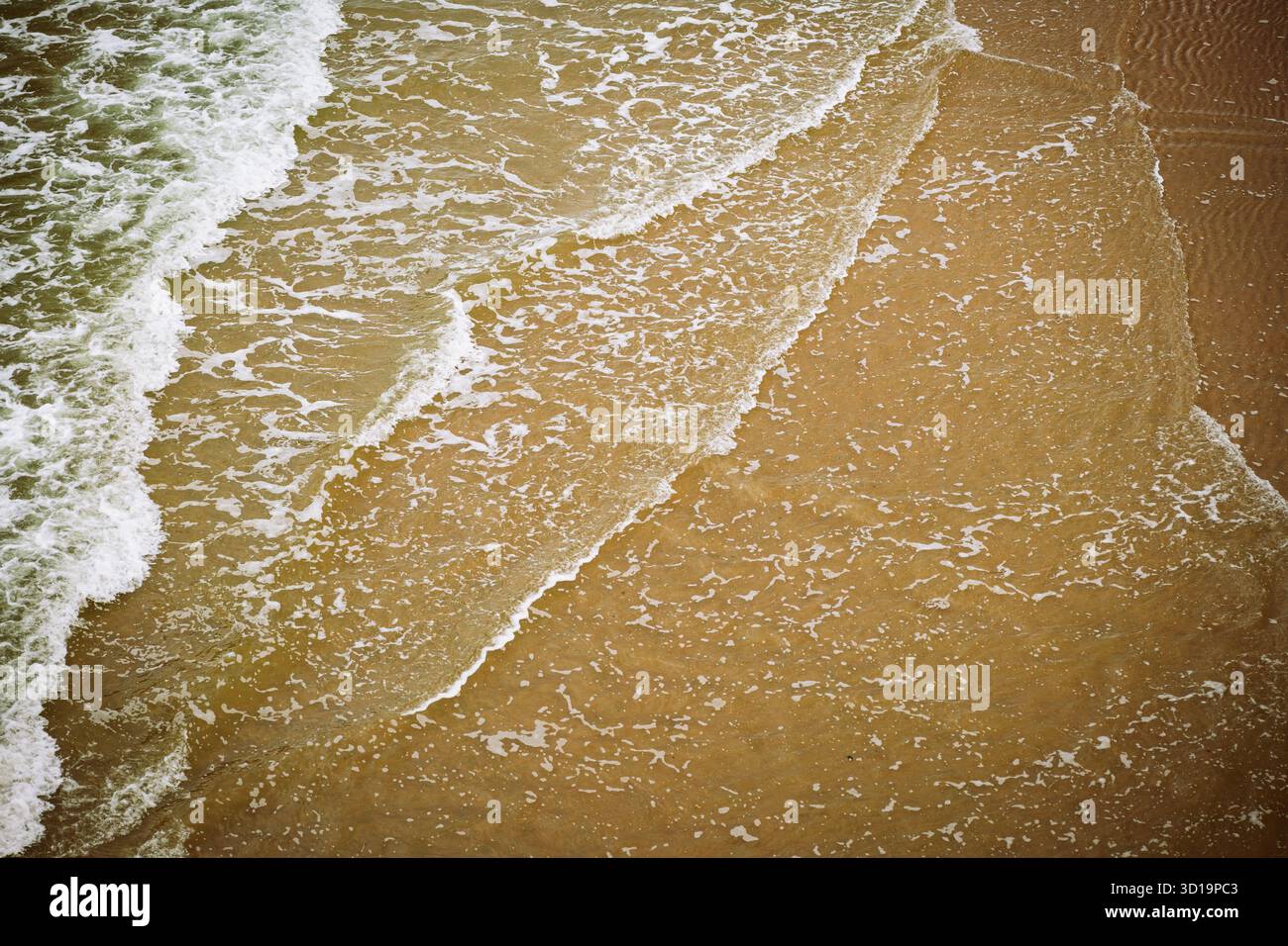 Foamy, shallow, tidal waves reaching the sandy shore. Top down view ...