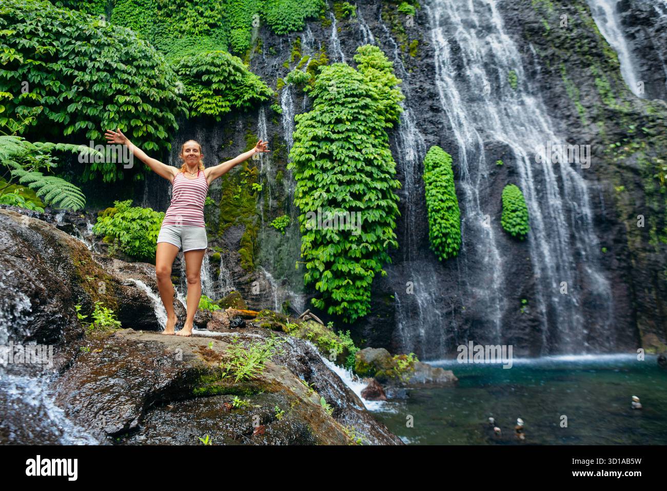 Woman rising hands up, stand in natural pool below Banyumala Twin ...