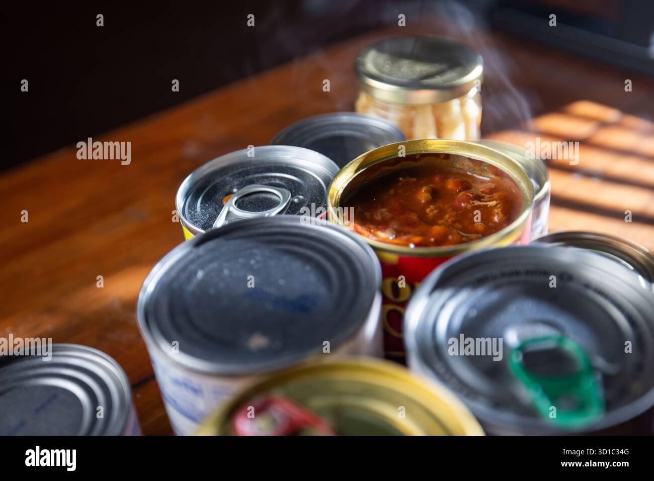 cans of food on a table and an open can of chilly with steam coning out ...