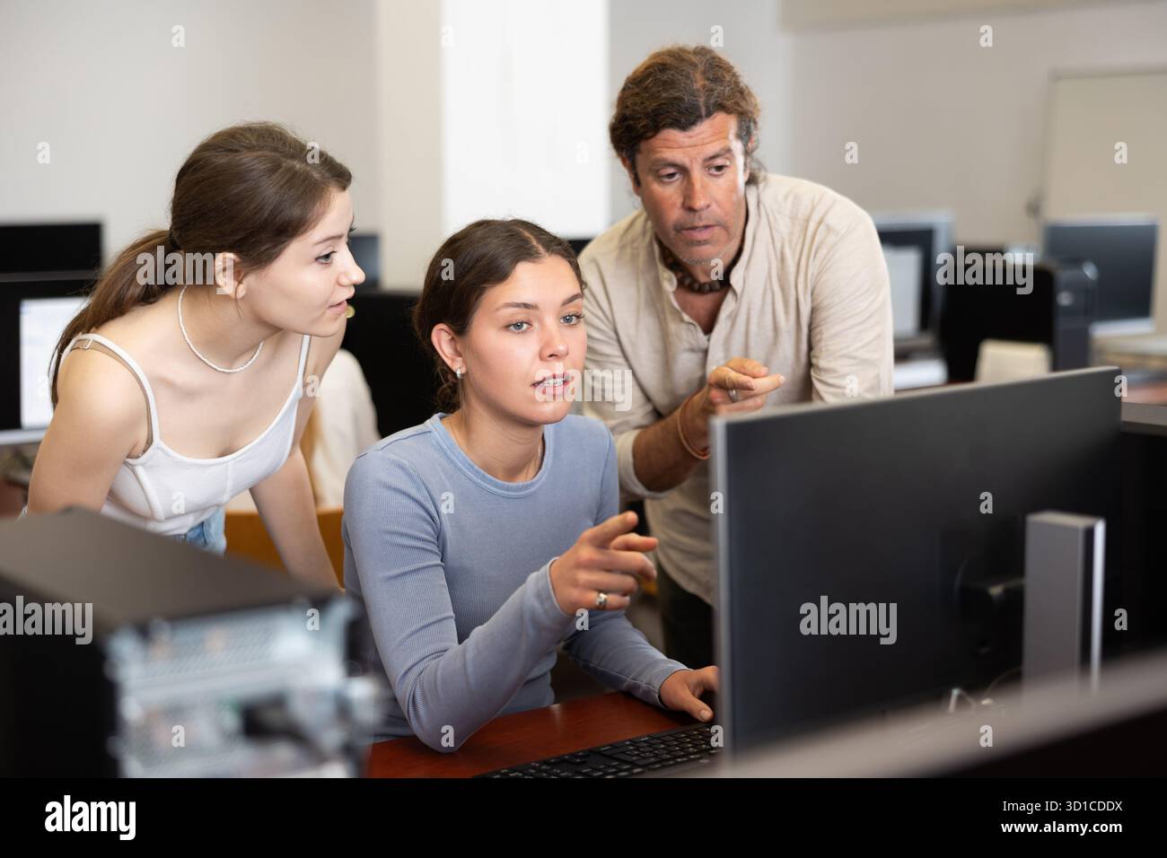 During computer lesson, two companions help girl student complete ...