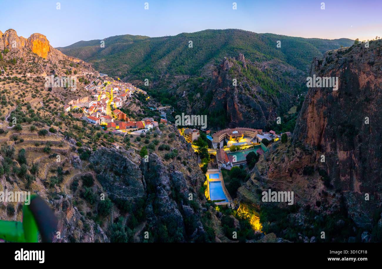 A panoramic view of a village nestled in a rocky gorge at dusk, with ...