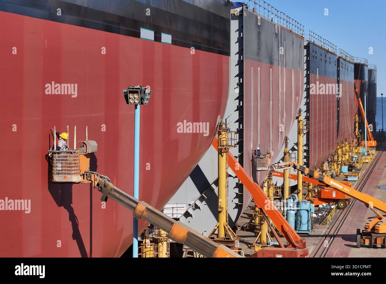 Workers build large ship hull sections on an aerial work platform at a ...